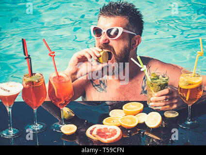 Cocktail with fruit at bearded man in pool. Man swimming and drink ...