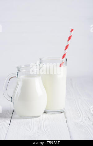 Glass of milk with stripped red paper straw and jug of milk on white ...