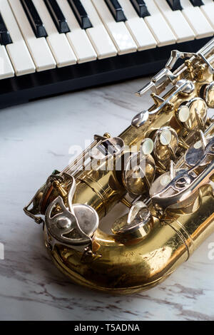 Rusty old classical saxophone on marble table next to electric piano ...