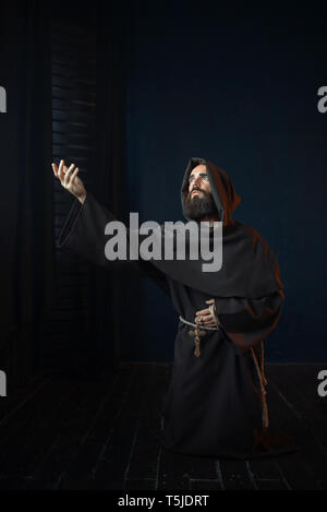 Medieval monk kneeling and praying, religion. Mysterious friar in dark ...