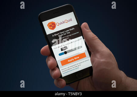 A man looks at his iPhone which displays the Quick Quid logo (Editorial ...