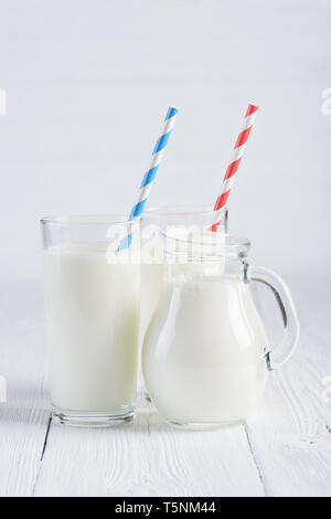 Glass of milk with stripped red paper straw and jug of milk on white ...