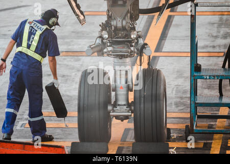 Asian ground crew perform safety inspection of an aircraft landing gear ...