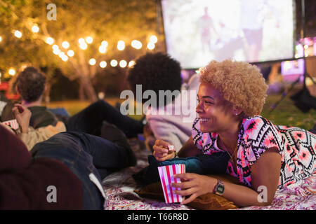Young woman with popcorn watching movie on sofa against blue background ...