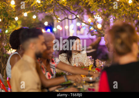 Friends enjoying dinner garden party under trees with fairy lights ...