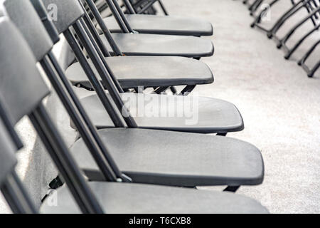 rows of empty black folding chairs in a large event hall with dark ...
