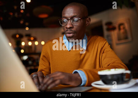 Warm toned portrait of contemporary African-American man using laptop ...