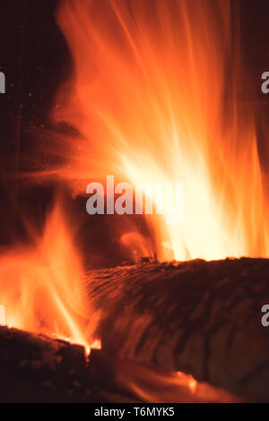 Large log on fire with flames and hot cinders and ash below. Detail ...