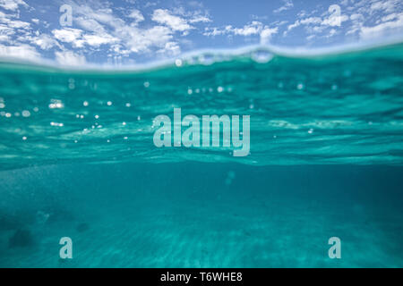 A split level shot of turquoise ocean water and clouds in a blue sky ...