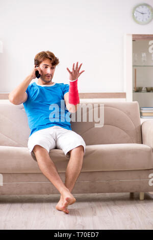 Young man with injured arm sitting on the sofa Stock Photo - Alamy