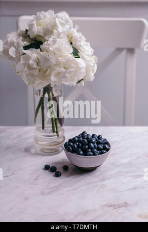 Fresh blueberries in white ceramic bowl on light stone surface with ...