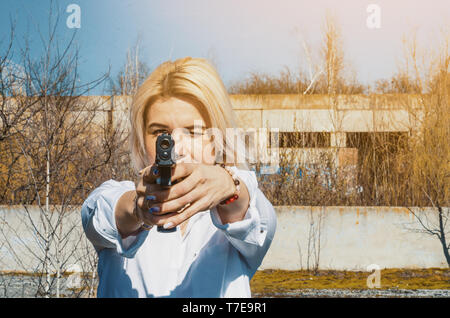 serious young woman with gun aiming on dark background, monochrome ...