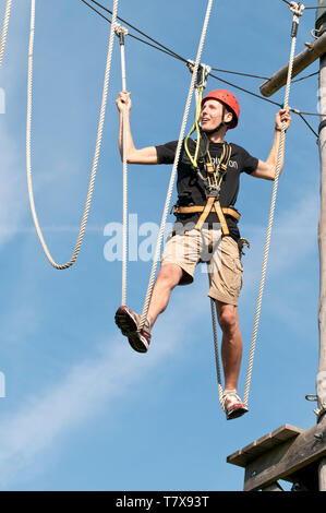 Young man has fun while absolving an balance exercise in high ropes ...