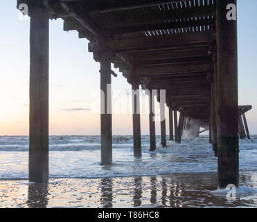 Sunrise at Claremont Pier with waves breaking over the super-structure ...