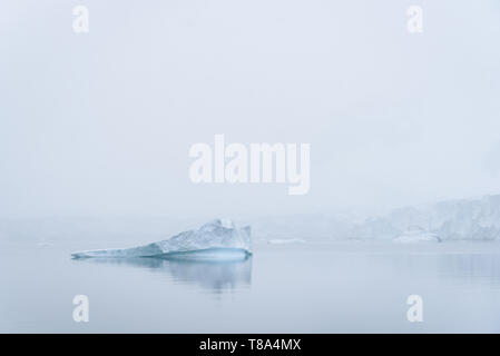 Sculptural iceberg shrouded in fog and floating in the waters of ...