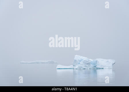 Sculptural iceberg shrouded in fog and floating in the waters of ...