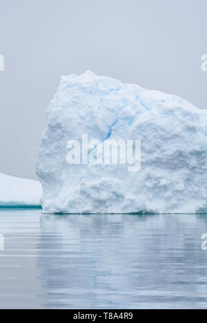 Sculptural iceberg shrouded in fog and floating in the waters of ...
