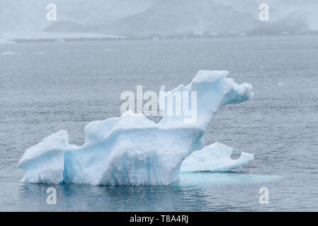 Sculptural iceberg shrouded in fog and floating in the waters of ...