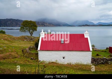 White cottage with a red roof, on the banks of Loch Shieldaig in Wester ...