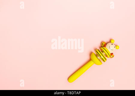 Yellow wooden baby rattle with bells over pink background. Mock up ...