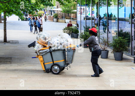 A female council street cleaner with a trolley emptying a rubbish bin ...