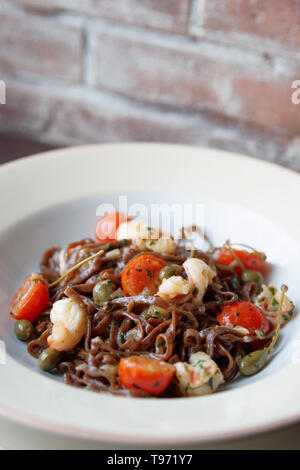 Rye pasta with capers and prawns in white porcelain plate on restaurant ...