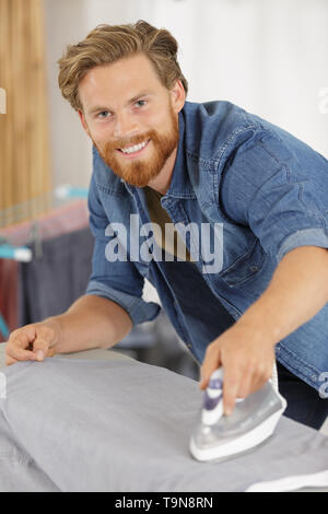 Young man with beard ironing clothes at home angry and mad screaming ...
