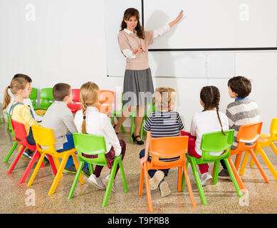 Friendly smiling teacher explaining studying material to children ...