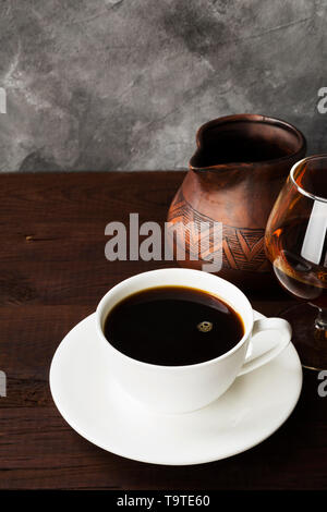 Coffee in white cup with cognac and clay cezve on wooden background ...