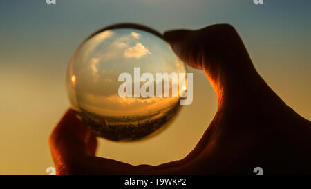 The hand holds glass ball which reflects sunset sky over city Stock ...