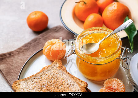 Jar of tasty tangerine jam and bread on light background Stock Photo ...