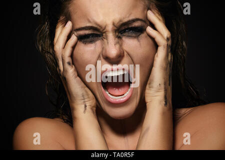 Sad and wet woman with smudged makeup on her face under the shower ...