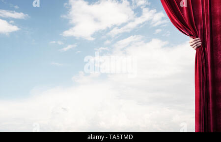 Cloudy landscape behind red curtain and hand holding it Stock Photo - Alamy