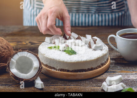 Confectioner decorates coconut raw cake with white pulp and mint on ...
