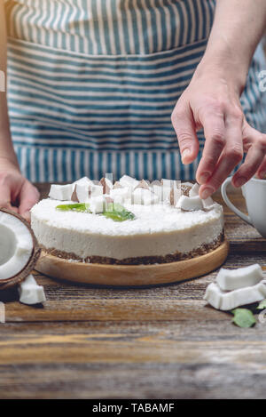 Confectioner decorates coconut raw cake with white pulp and mint on ...