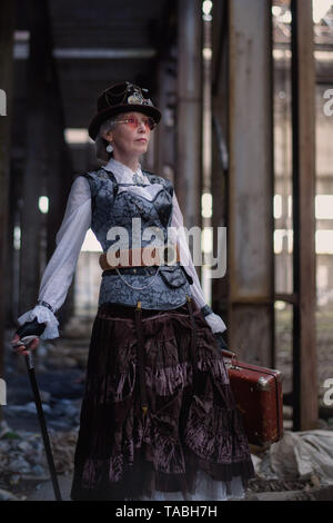 elderly lady in a steampunk costume at an abandoned factory with arms ...