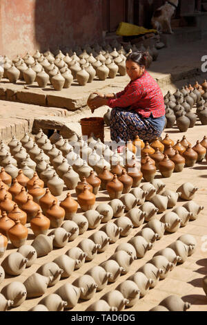 Woman dipping pottery into color as other clay products sun-dry near ...