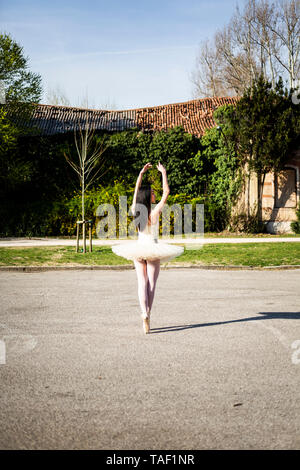 rear view of attractive ballerina in tutu exercising at ballet barre ...