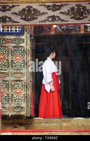 A shrine maiden in red and white robes in a courtyard at the ...