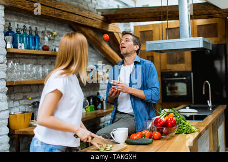 Lovely cheerful young couple cooking dinner together and having fun at ...