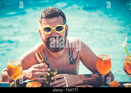 Cocktail with fruit at bearded man in pool. Man swimming and drink ...