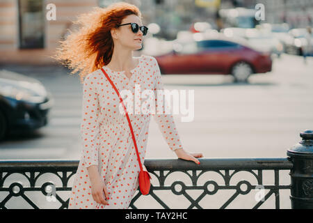 Red-haired woman with sunglasses laughing leaning against a tree on a ...