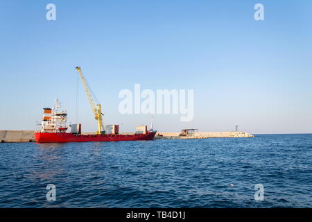 Yellow crane unloading sand from large freighter cargo ship in harbor ...