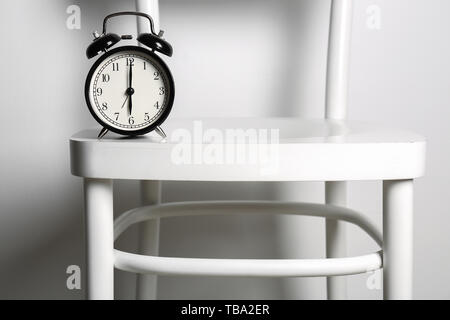 Alarm clock on chair against white background Stock Photo - Alamy
