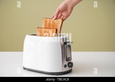 Woman taking bread slice from white toaster near wooden wall Stock Photo - Alamy