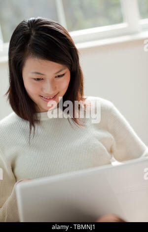 Smiling Asian woman using digital tablet near window at home for remote ...