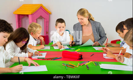 Female teacher helping schoolkids drawing with color pencils in ...