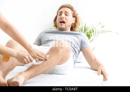Man suffering from pain during wax epilation of legs in beauty salon ...