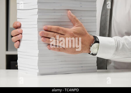 Businessman working at an office, reads stack of books and reports ...