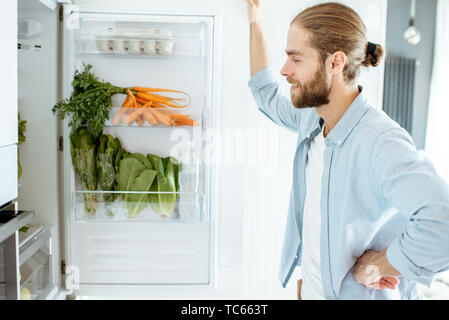 Adult man standing at refrigerator, choosing frozen convenience food in ...
